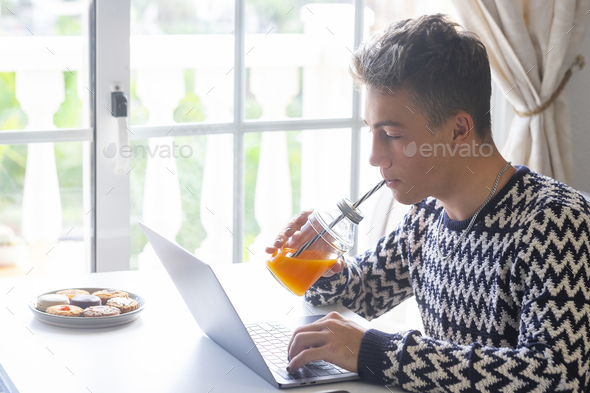 Beautiful teenager drinking an orange juice using laptop at home in ...