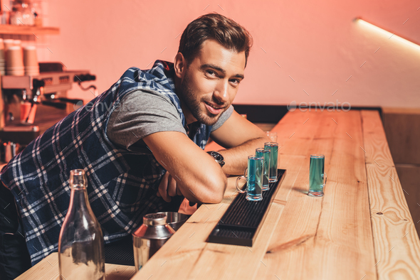 side view of young barman looking at camera while standing at counter ...