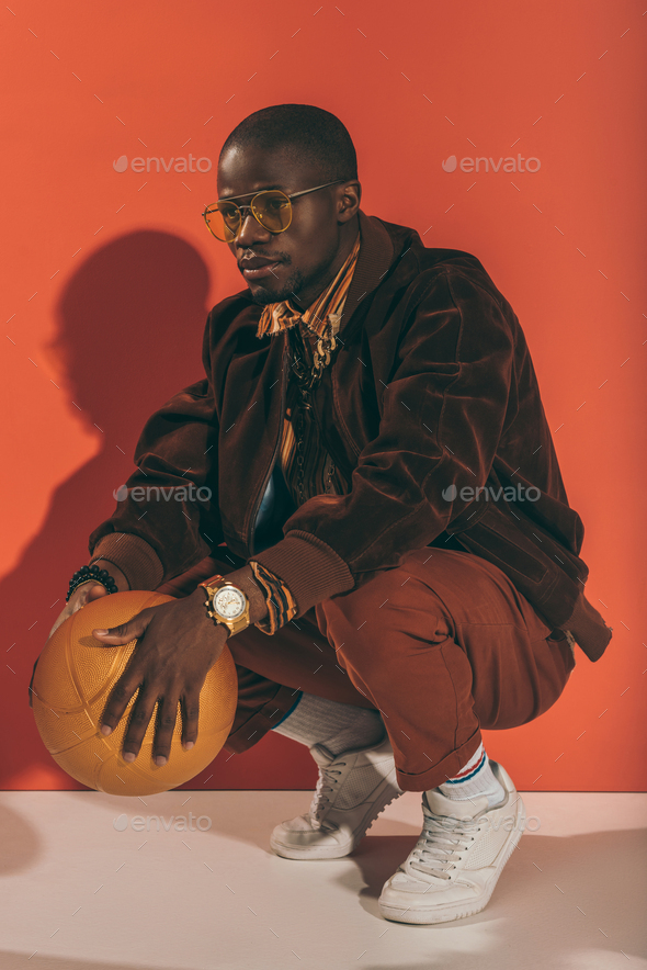 stylish african american man crouching and holding golden basketball ...