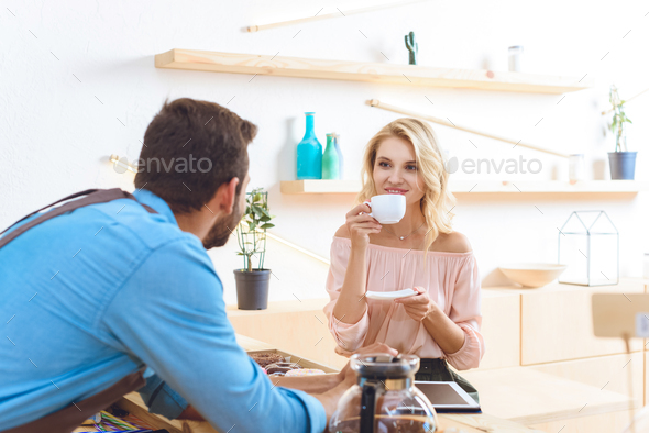 back view of barista looking at beautiful woman drinking coffee in cafe ...
