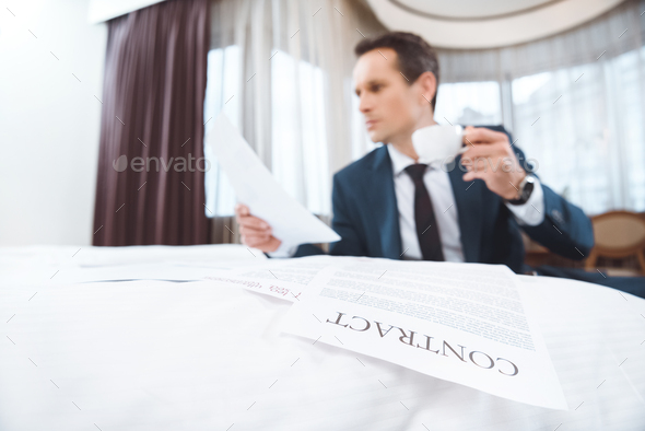 Young businessman in formal suit sitting in hotel room and reading some ...