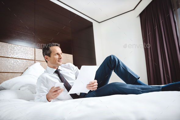 Smiling businessman in formal suit lying on hotel room bed while ...