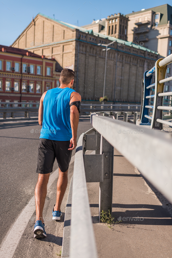 rear view of athletic sportsman in sportswear training and running in ...