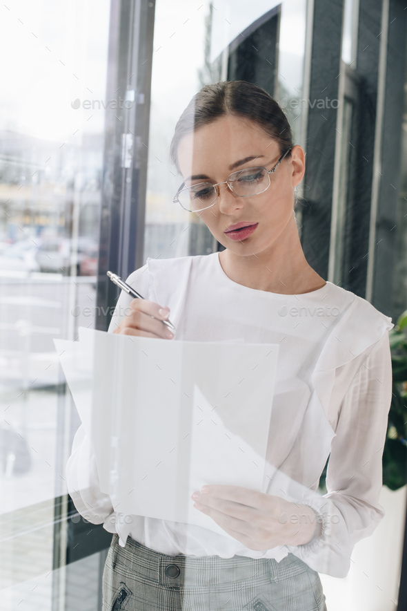 Young businesswoman standing in front of window and working with some ...