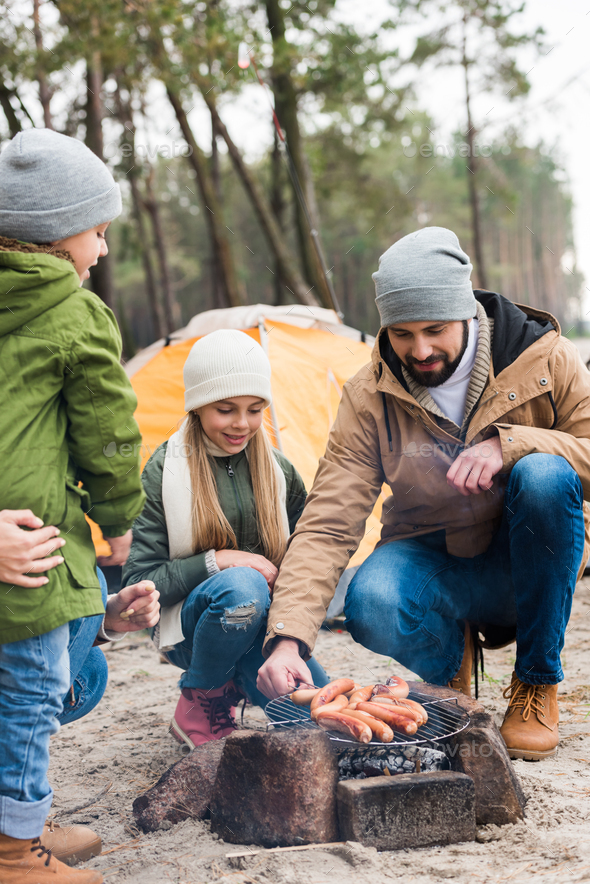 father and kids grilling sausages on nature while having hiking trip ...