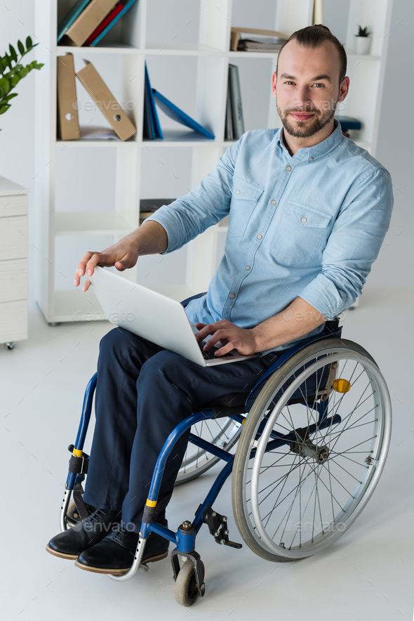 smiling disabled businessman in wheelchair working with laptop in ...