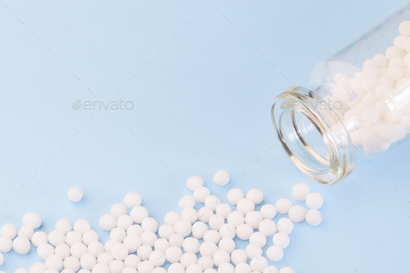 Homeopathic globules and glass bottle on blue background. Alternative ...