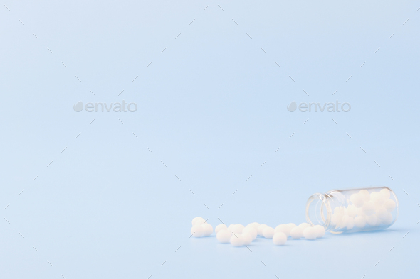 Homeopathic globules and glass bottle on blue background. Alternative ...