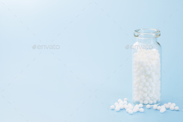 Homeopathic globules and glass bottle on blue background. Alternative ...