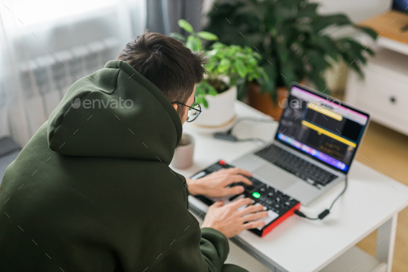 Man music producer or arranger using laptop and midi keyboard and other ...