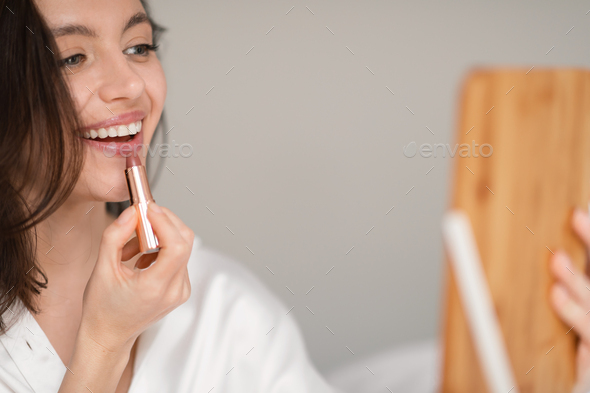Smiling caucasian millennial woman applying lipstick on lips, looking ...
