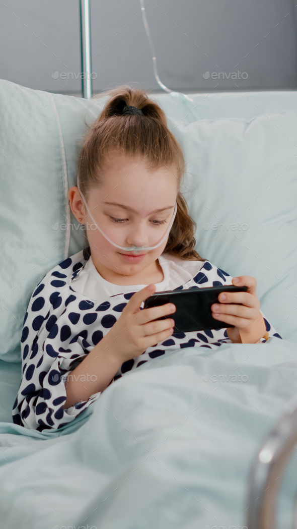 Sick little child resting in bed playing online video games using ...