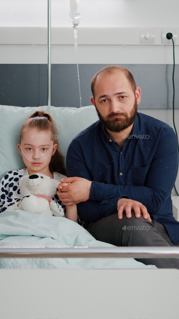 Portrait of sad father holding sick child hands looking into camera ...