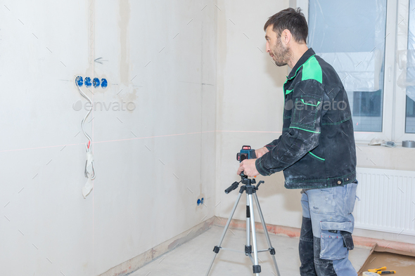 Man makes repairs in new apartment. Builder levels walls using laser ...