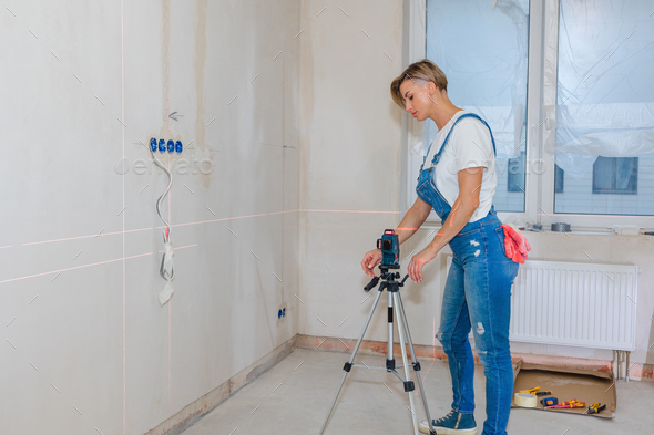 Woman makes repairs in new apartment. Builder levels walls using laser ...