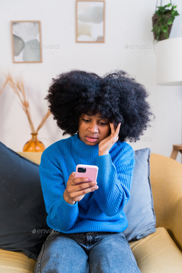 concerned Black woman using smartphone on sofa Stock Photo by ...