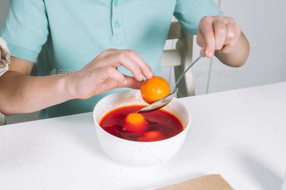 Cropped photo of boy hands, coloring orange Easter hen eggs in spoon ...