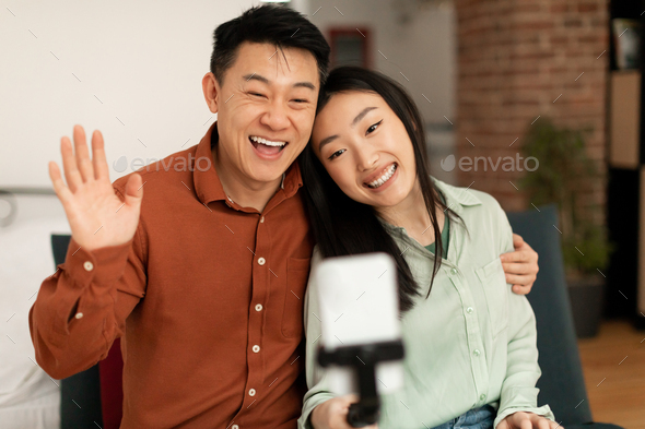 Happy asian spouses making video call via cellphone on tripod, man ...