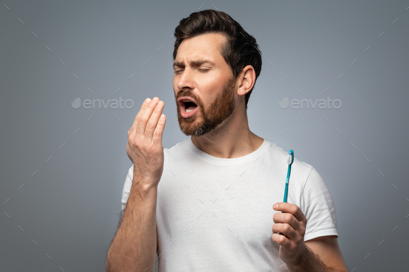 Bad breath. Handsome middle aged man checking his breath with his hand ...