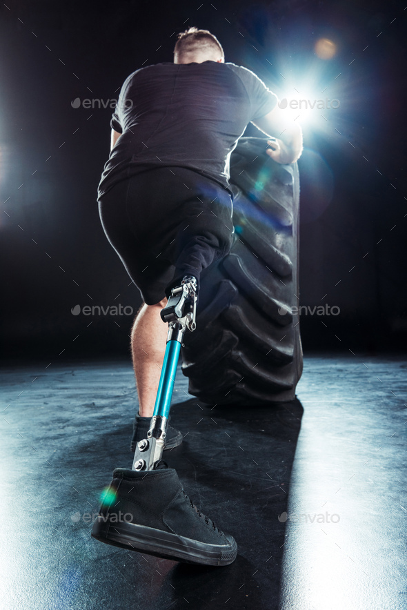 back view of paralympic sportsman with leg prosthesis pulling tire ...