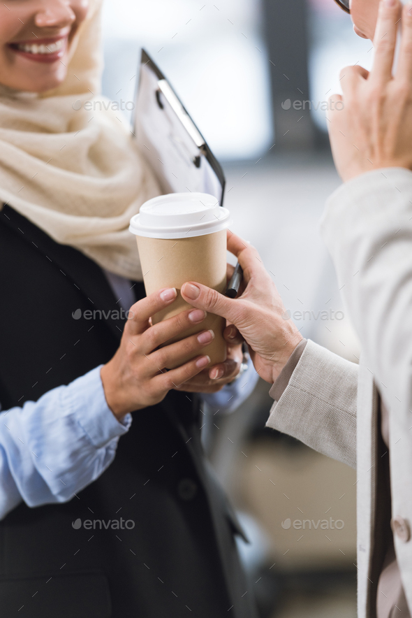 partial view of smiling businesswoman giving coffee to colleague at ...
