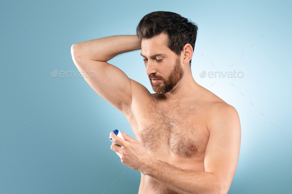 Shirtless handsome man spraying deodorant under arm for fragrance ...