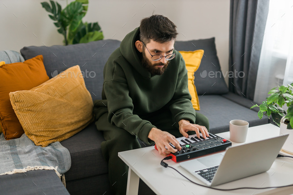 Man music producer or arranger using laptop and midi keyboard and other ...