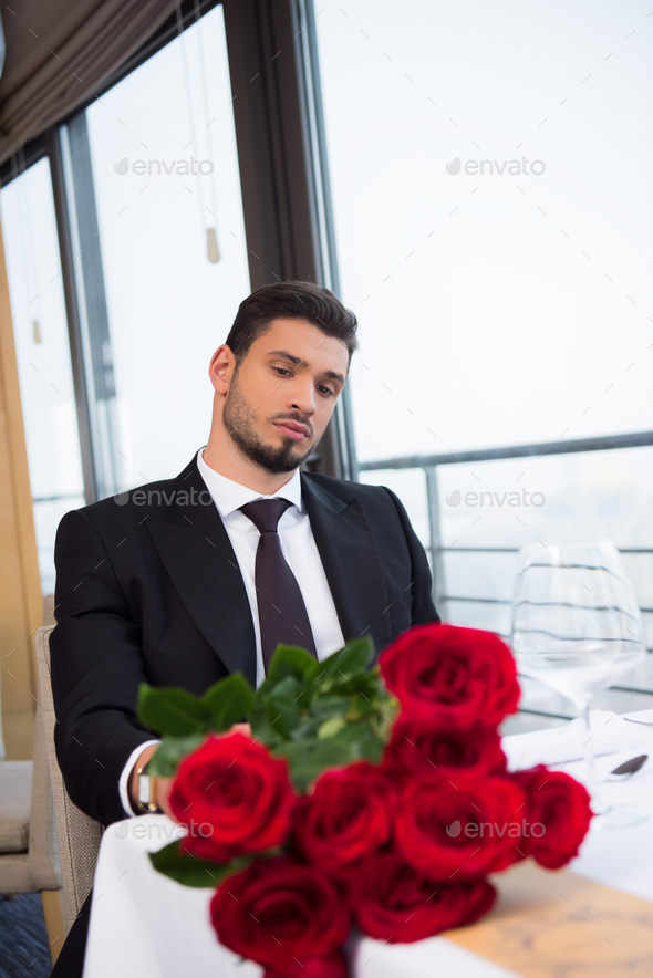 portrait of young man in suit with bouquet of red roses waiting for ...