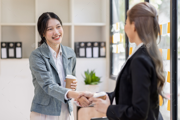 Two young asia business woman shaking hands successful making a deal ...