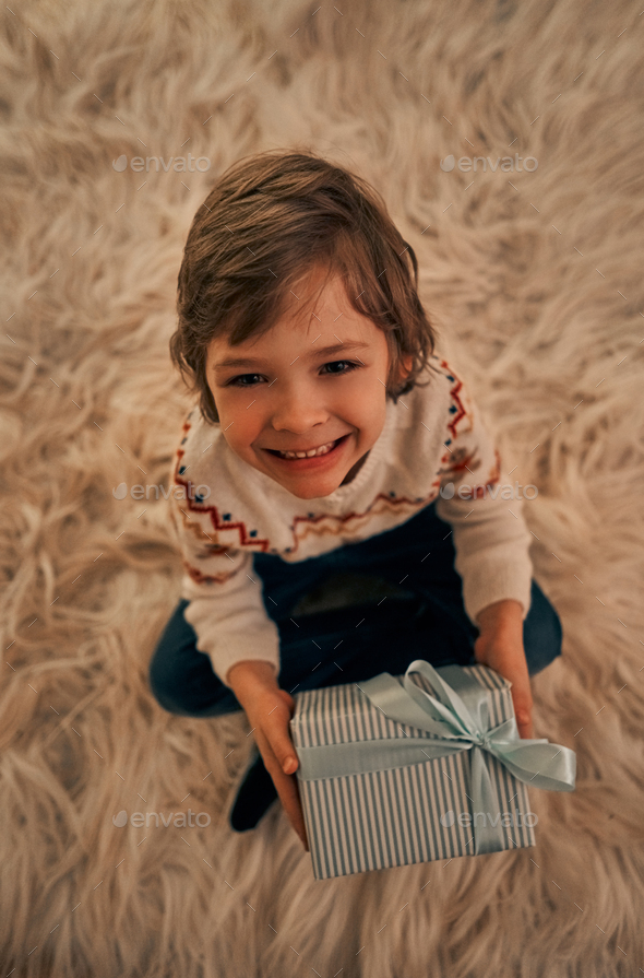 The cute boy with a gift box sitting on the floor Stock Photo by artemp3