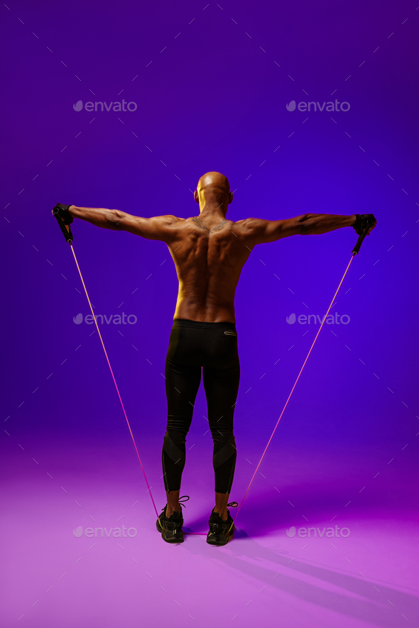 Back view of man performs exercises with expander on studio background ...