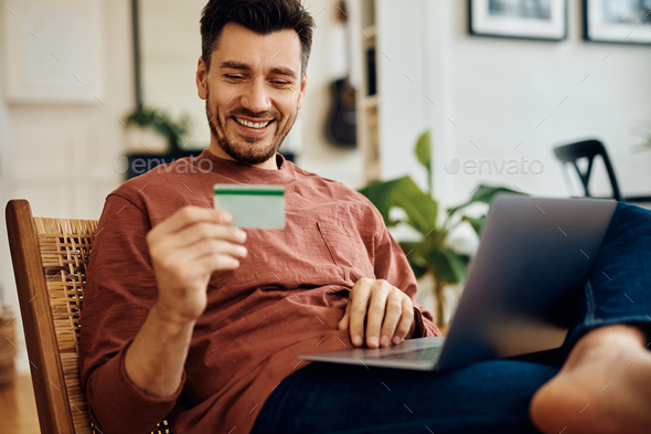Happy man using laptop and credit card for online banking from home ...