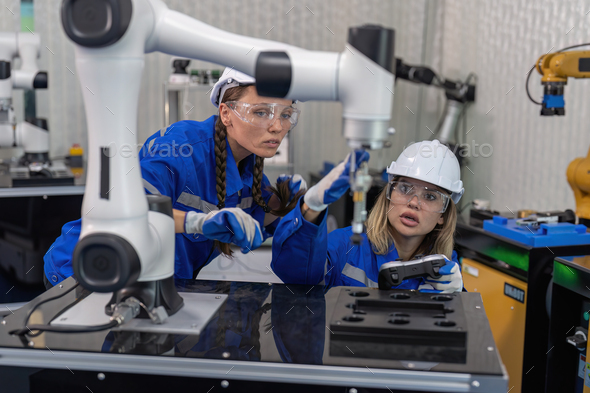 Female senior robotic engineer in modern factory teach new comer ...