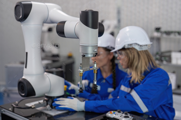 Female senior robotic engineer in modern factory teach new comer ...