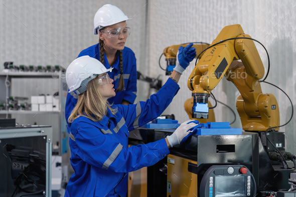 Female senior robotic engineer in modern factory teach new comer ...