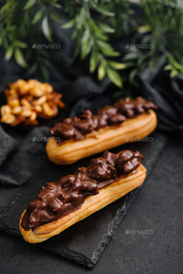Two eclairs with dark chocolate on black board Stock Photo by AntAlexStudio
