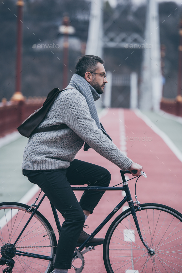 side view of handsome adult man riding bicycle on pedestrian bridge ...