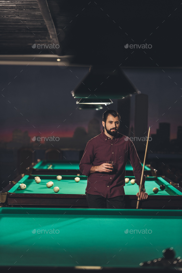 successful handsome man standing beside pool table with drink at bar ...