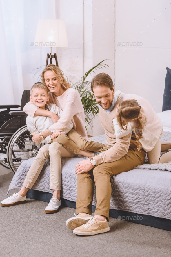 smiling father with disability and mother playing with children on bed ...