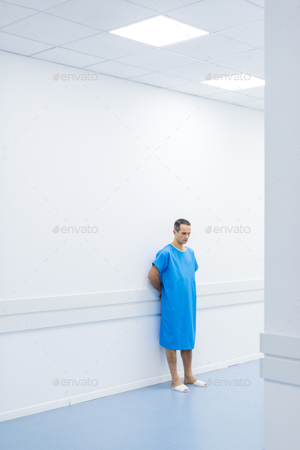 male patient in medical gown standing at wall in hospital Stock Photo ...