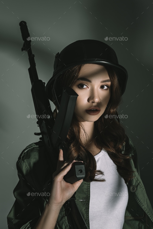 beautiful girl posing in military helmet with rifle, on grey with ...