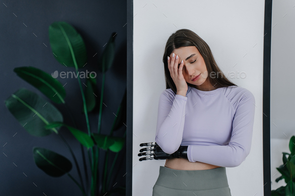 Exhausted beautiful young woman with bionic hand after workout touching ...
