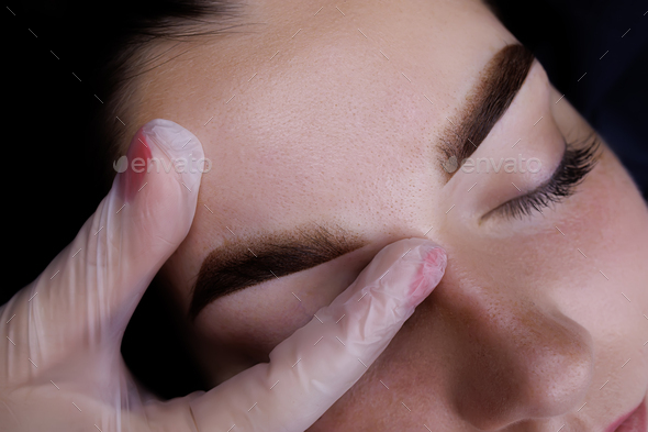 Permanent makeup of the eyebrows, the fingers of the master stretch the ...