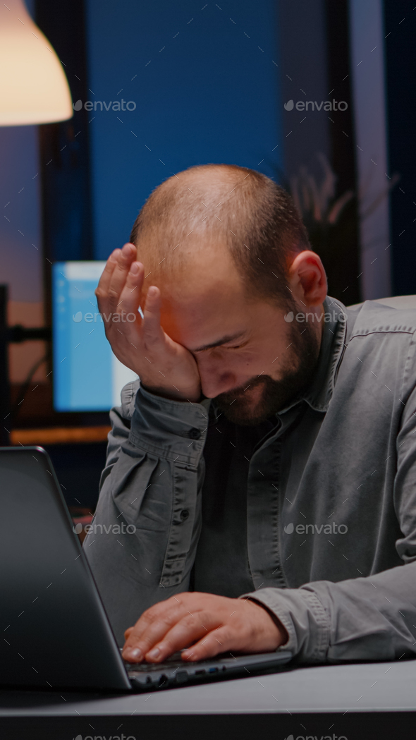 Overworked businessman rubbing face while working at financial ...