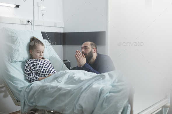 Young sad desperate father praying for sick little girl under treatment Stock Photo by DC_Studio
