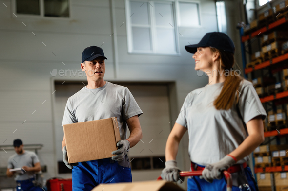 Two workers communicating while carrying packages in a warehouse. Stock ...