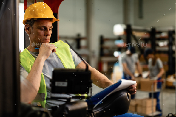 Forklift driver going through paperwork in industrial warehouse. Stock ...