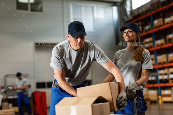 Warehouse worker assisting female colleague with packages in industrial ...