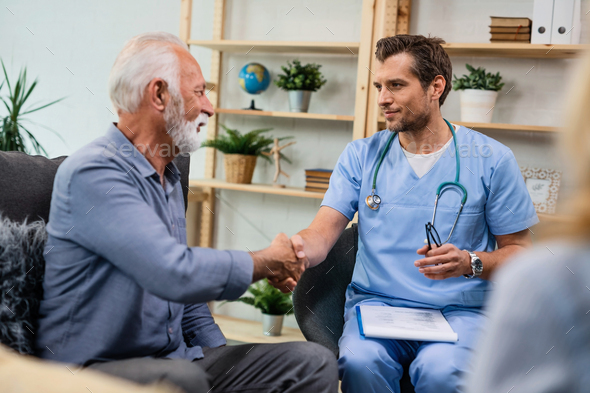 General practitioner handshaking with senior man while being in a home ...