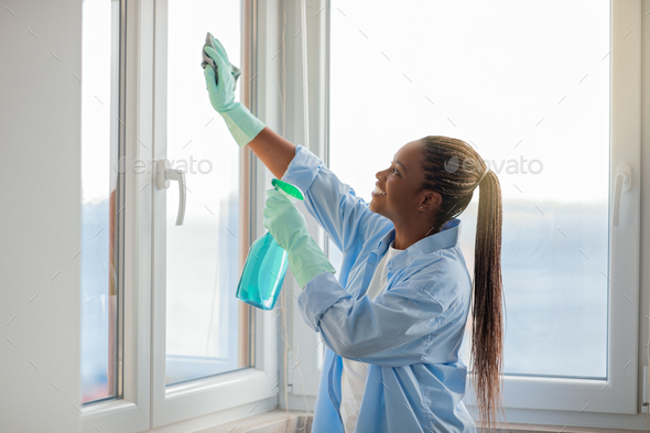 Happy young black woman housekeeper cleaning windows at apartment Stock ...
